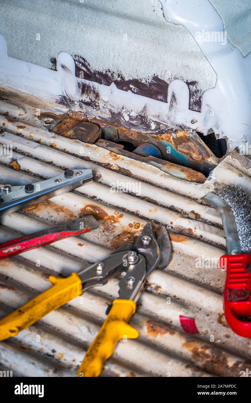 Rusty hole in vehicle floor with tools in the foreground, tin scissors ...