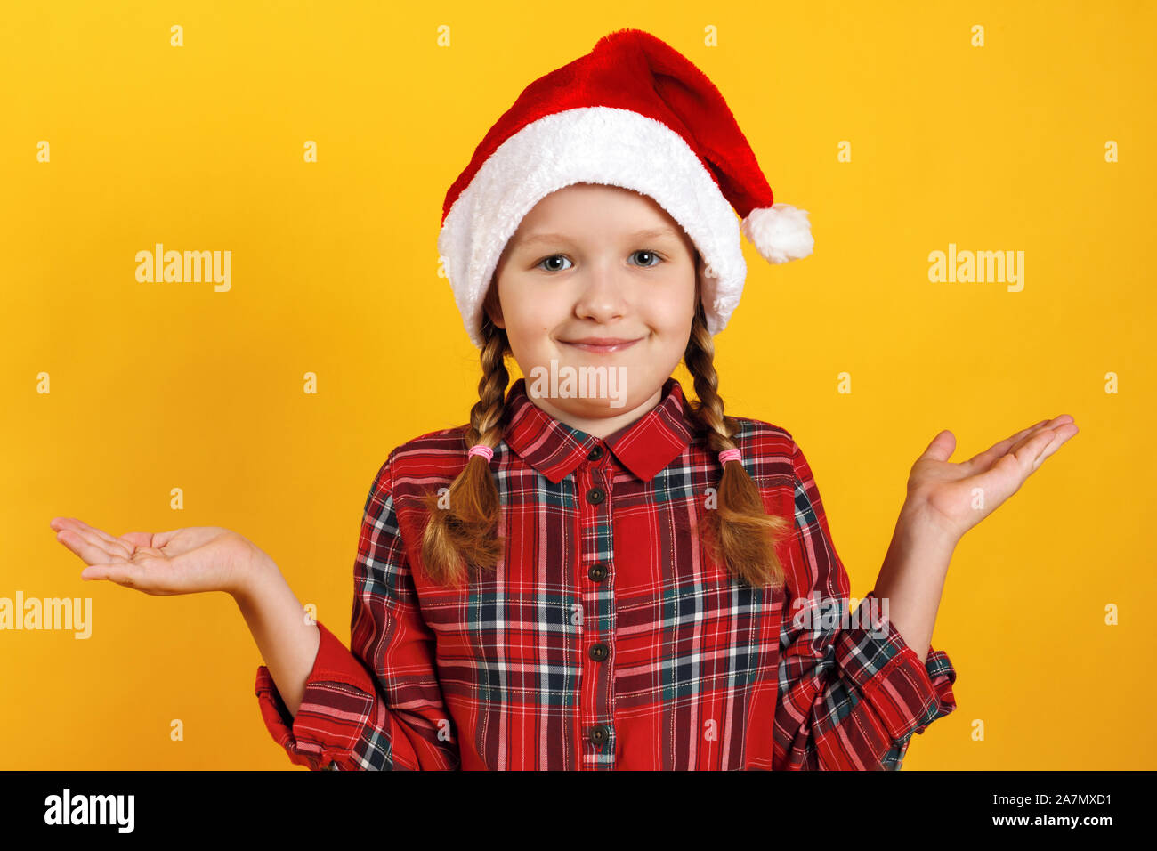 Cute little girl in santa hat shrugs. Close-up of a child waiting for ...