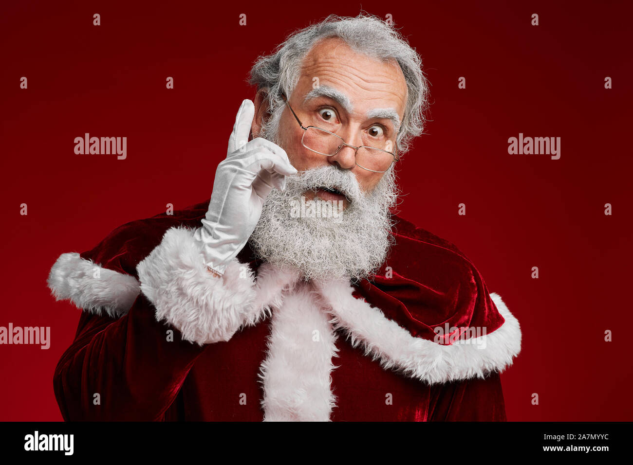 Portrait of surprised Santa Claus pointing up while posing against red ...