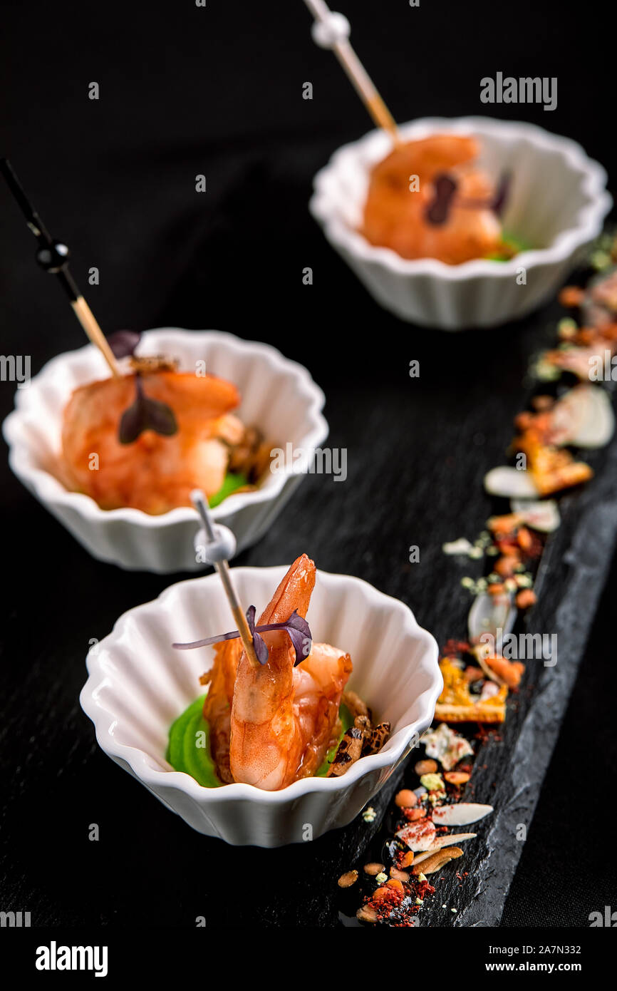 Canapes with tiger prawns on a skewer on a black background. The ...
