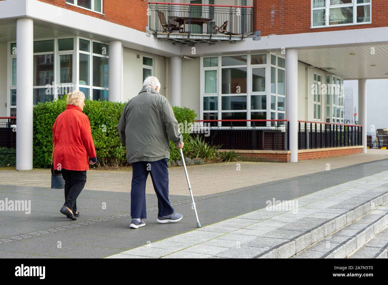 An elderly couple walking together with the man using a walking stick ...