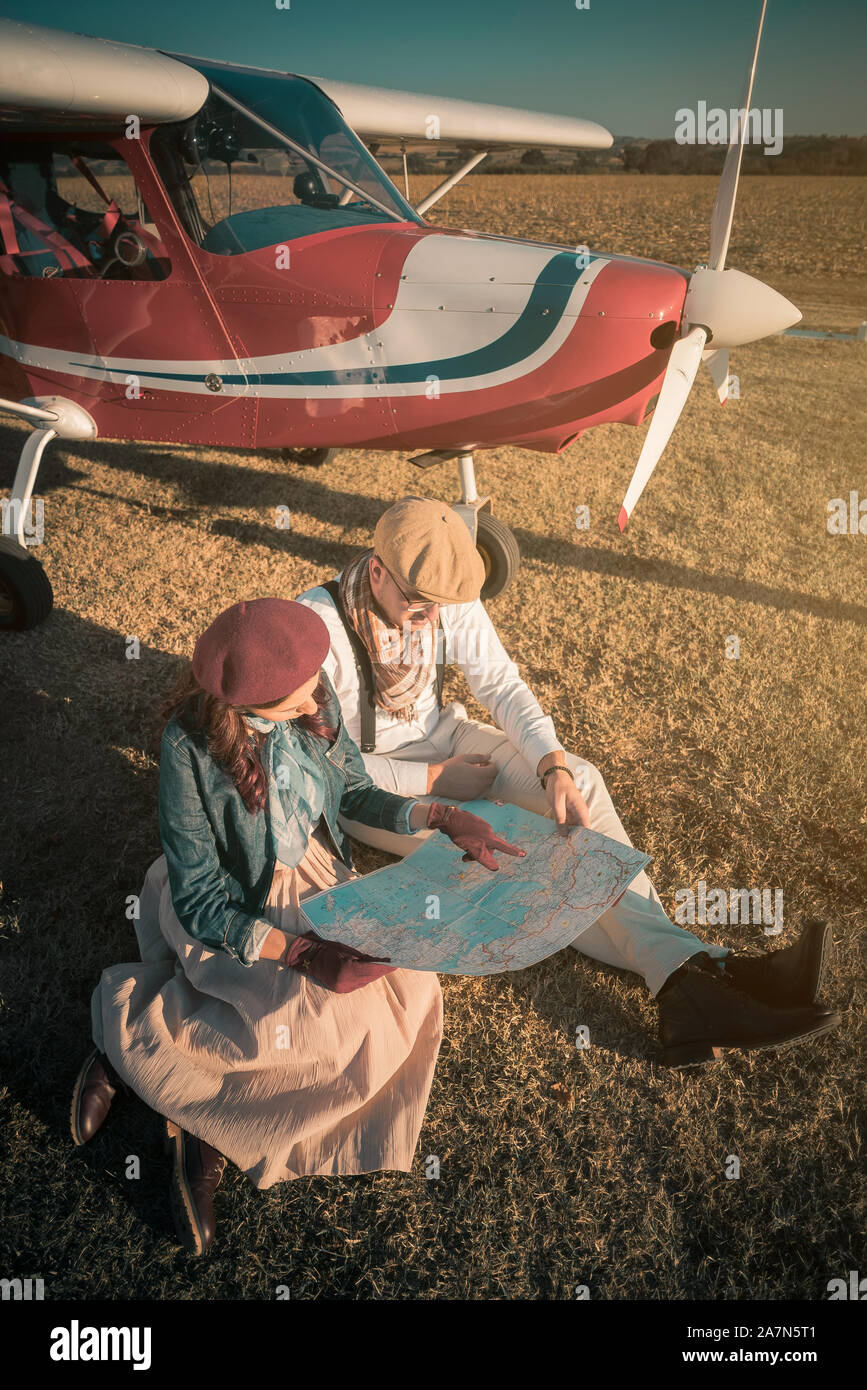 Young retro tourists looking on map by the small plane on airfield high ...