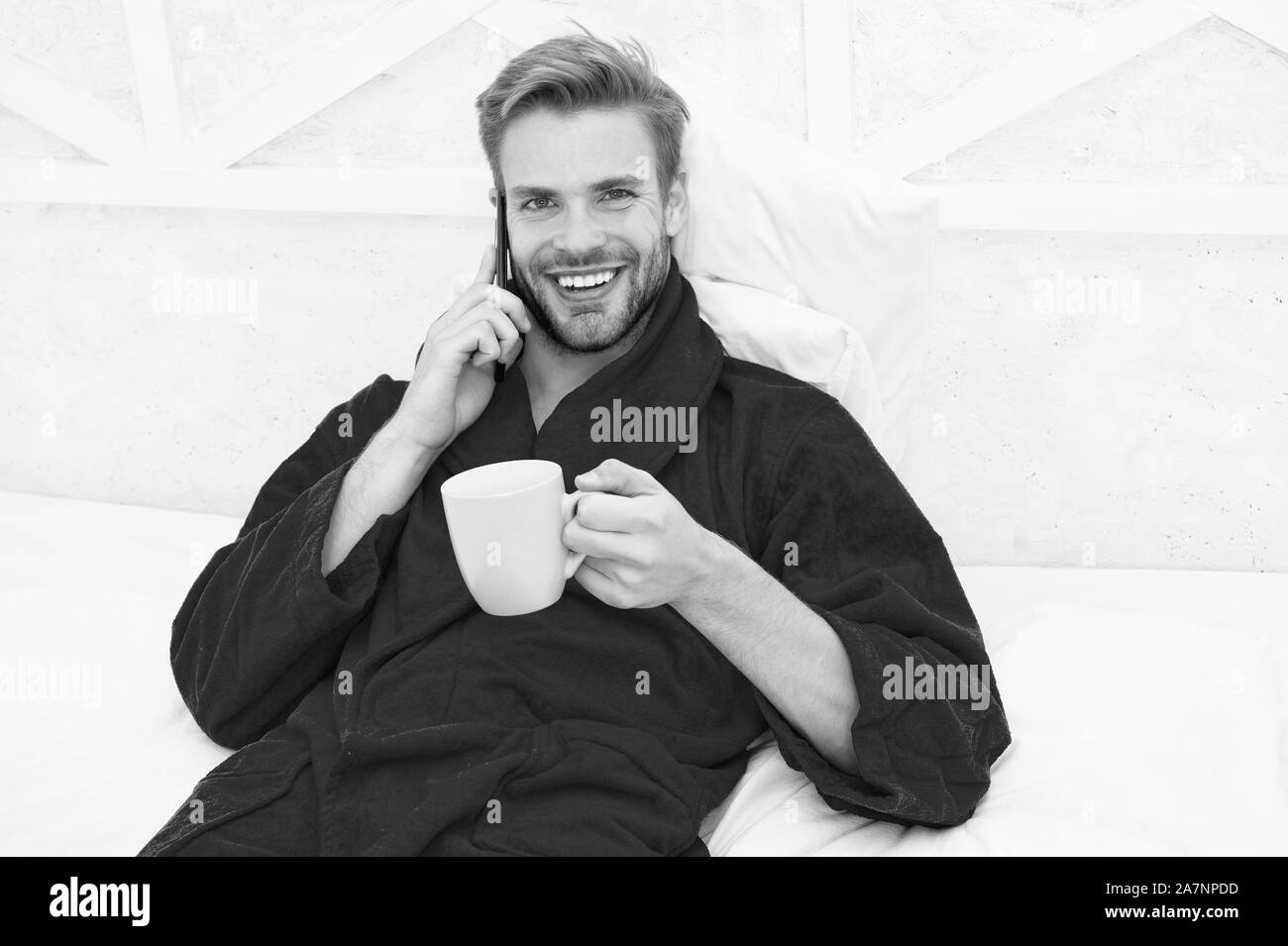 Break time. Happy guy in bathrobe relaxing during break in bed ...
