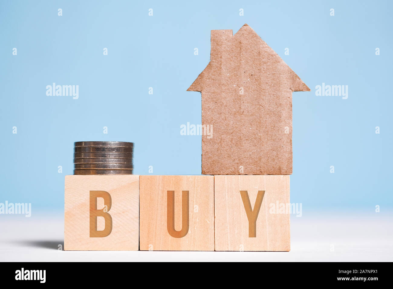 Abstract cardboard house next to coins, the word buy on cubes. The ...