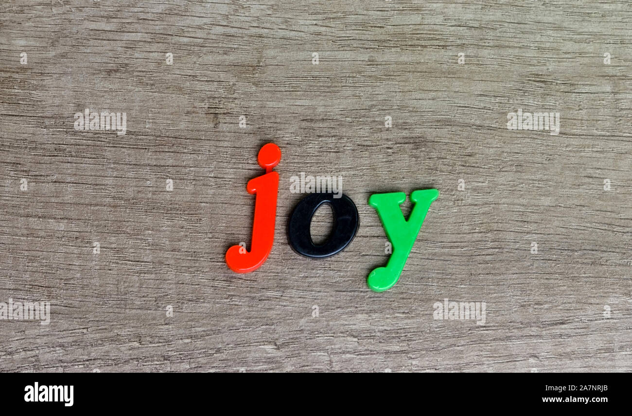 Joy word written with plastic multi colored letters on a wooden table ...