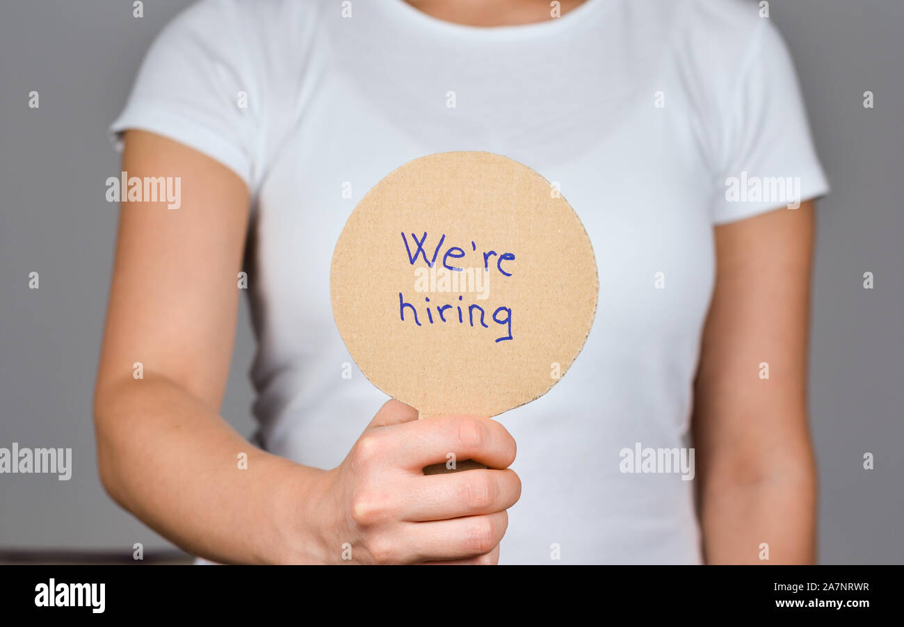 Young women showing round cardboard paper with handwritten text - We're ...