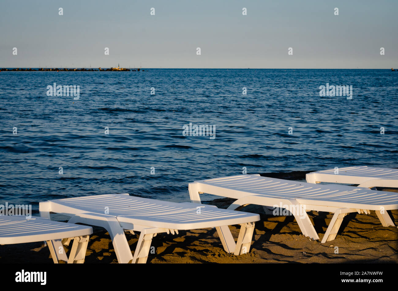 Empty white plastic sunbeds set on the seafront, during summer season ...