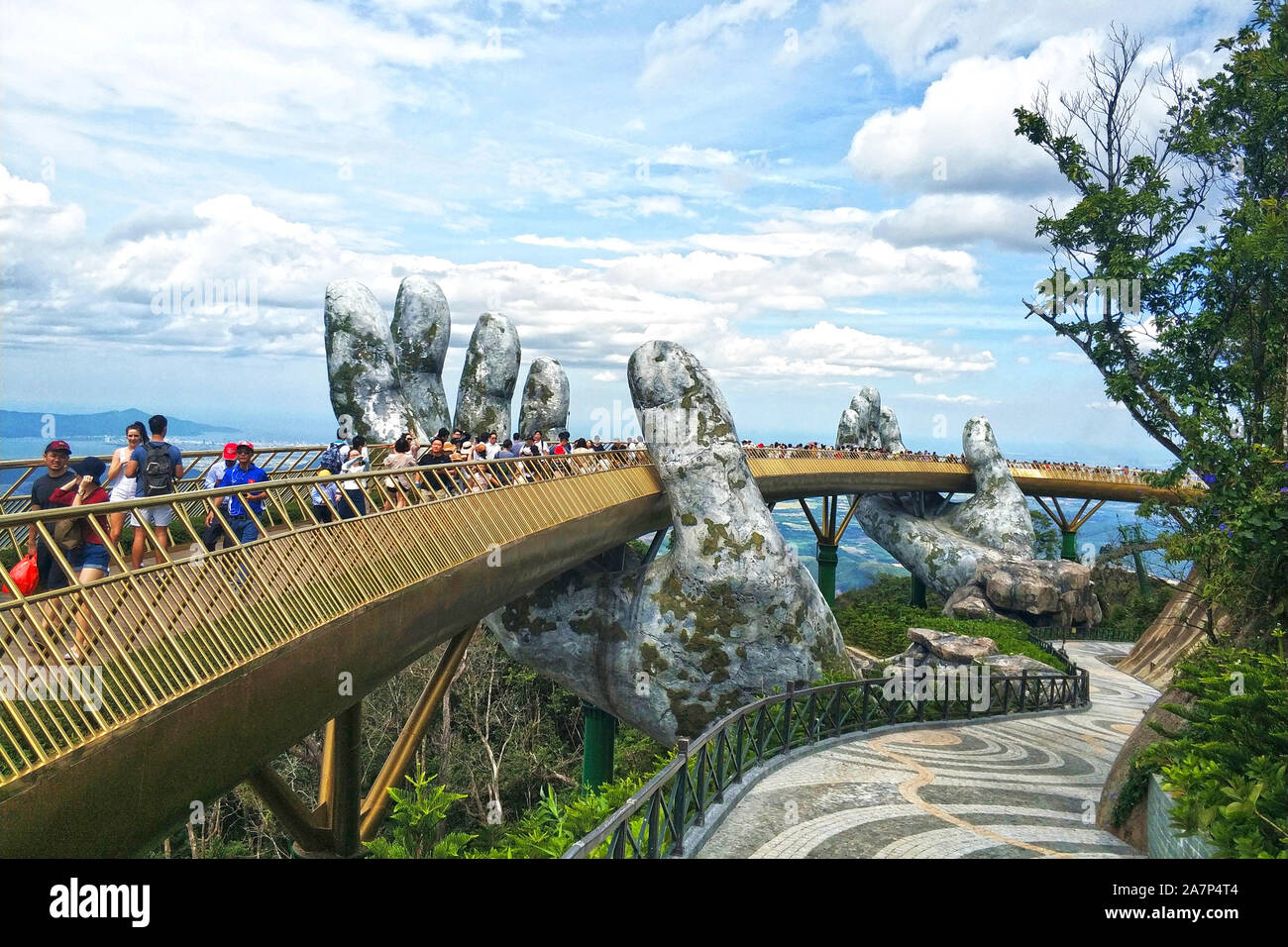 Tourists visit the Golden Bridge held up by hand statues surrounded by ...