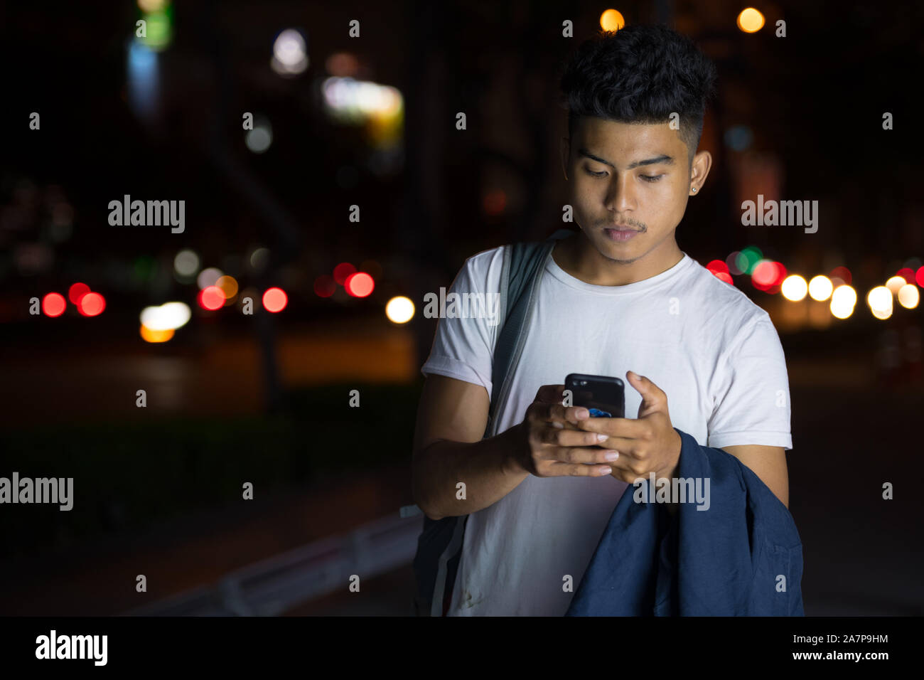 Young Asian man using phone in the city streets at night Stock Photo ...