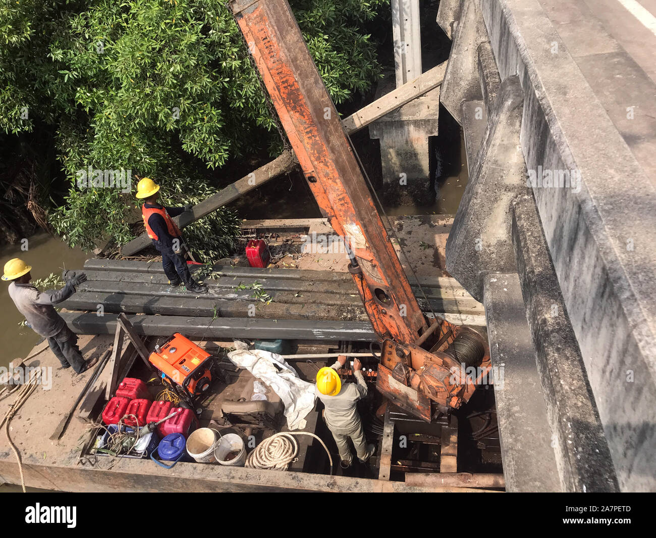 Team of workers pull the concrete pillars out of the water on the iron ...