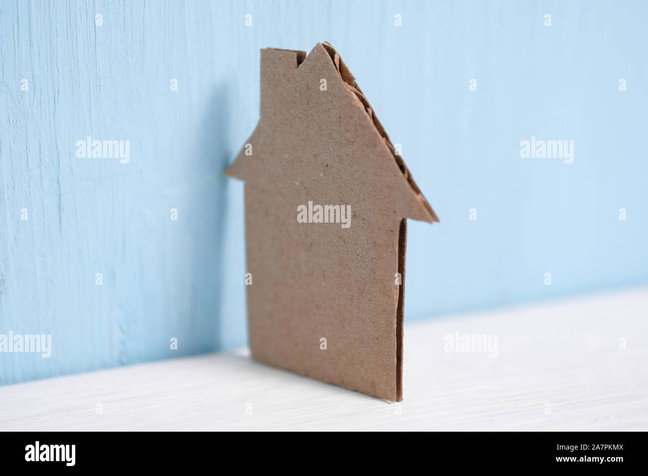 Cardboard cutout house leaned against the wall on blue background. The ...