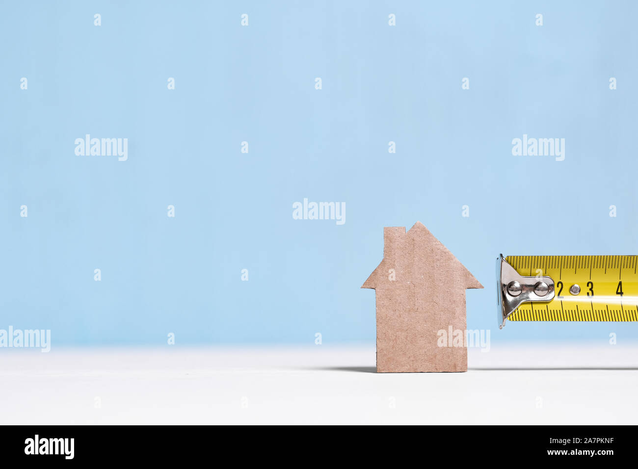 Metal measuring tape and cardboard cutout house on blue background with ...