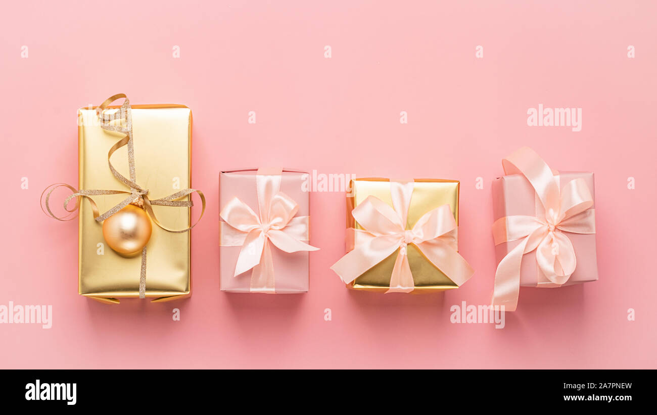 Festive boxes with satin ribbon bow golden toy balls on a pastel pink ...