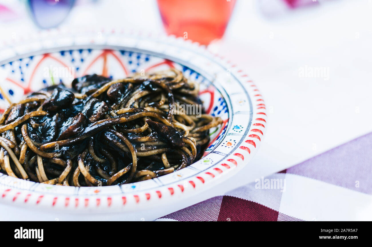 Black squid ink pasta on the plate with red-blue pattern in the ...