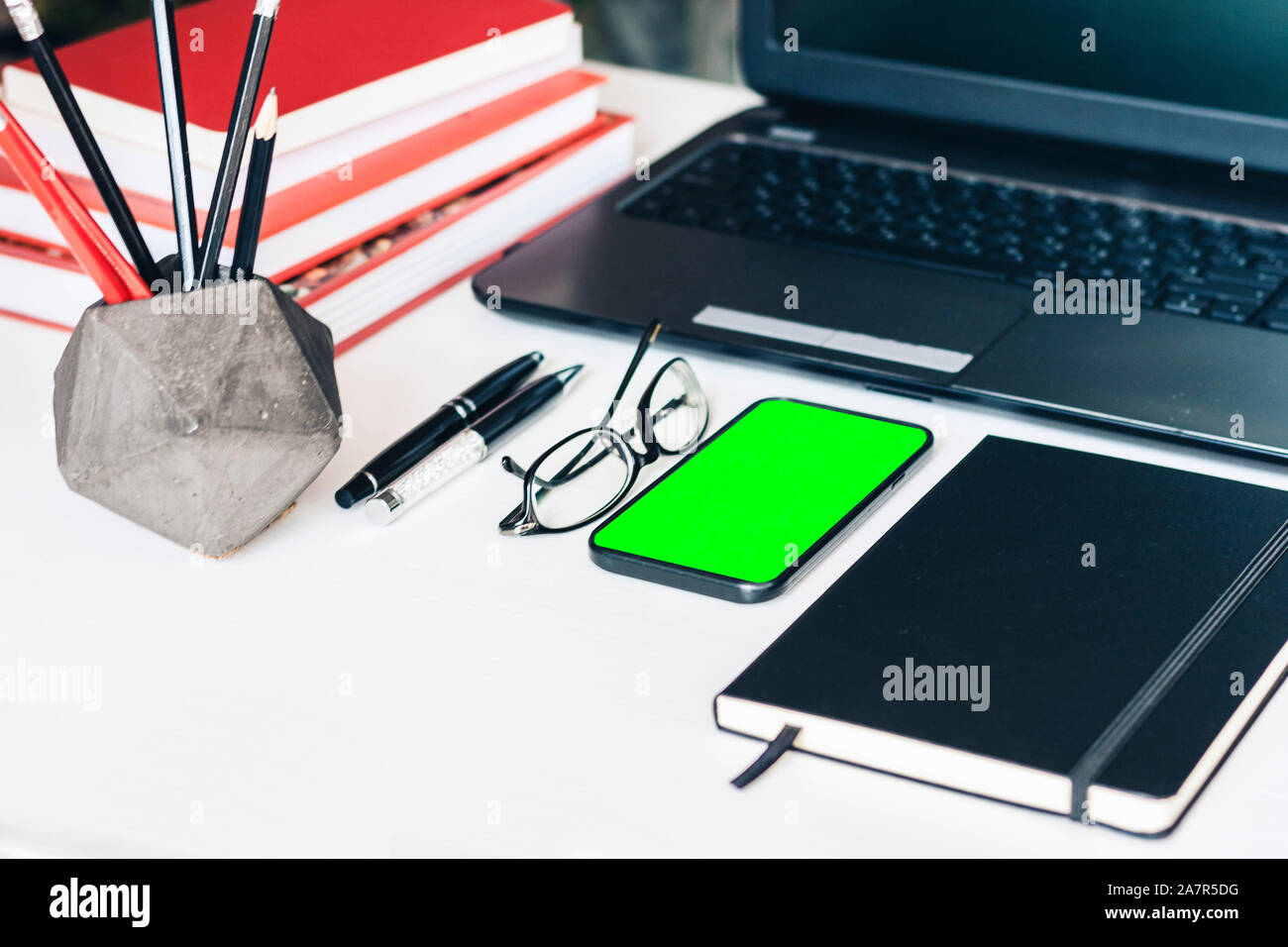 Stack of books, green screen smartphone, laptop, notebook, pencils in ...