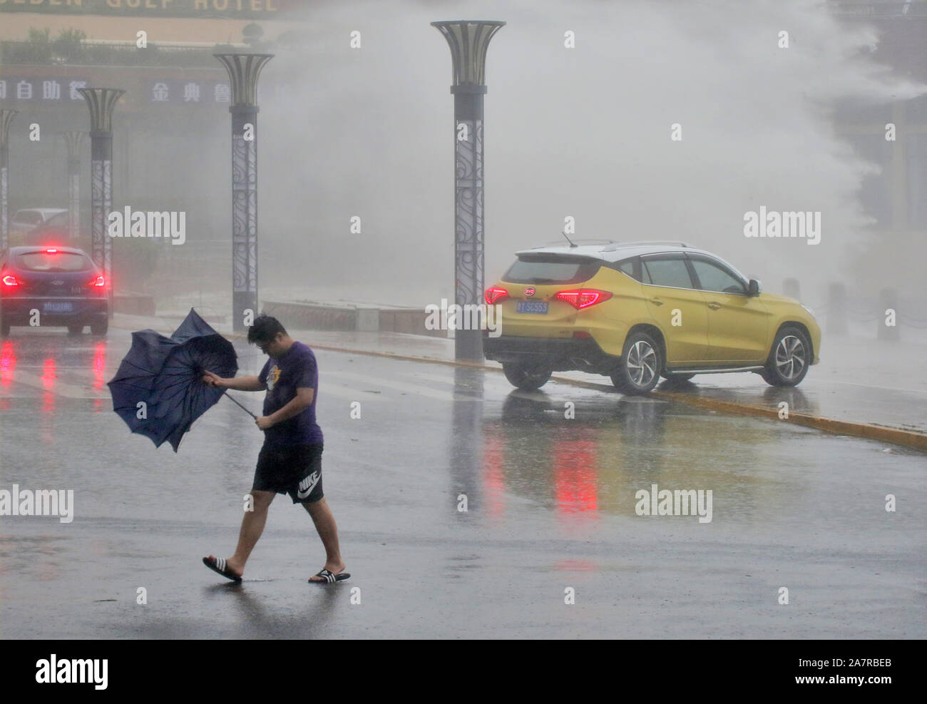 A local resident struggles with his umbrella in heavy rain and strong ...
