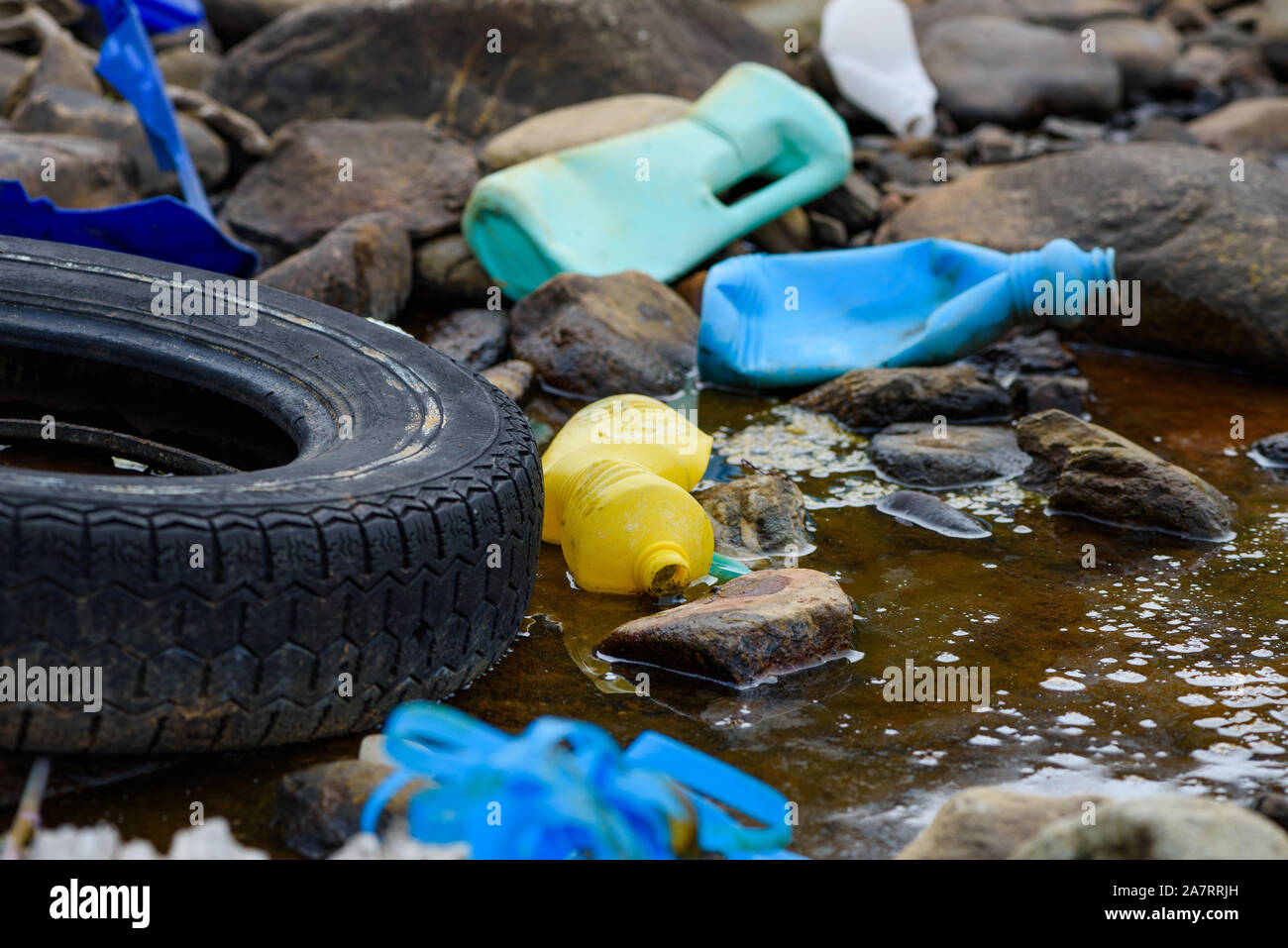 Enviromental pollution. Rubber tire with plastic waste in dirty water ...