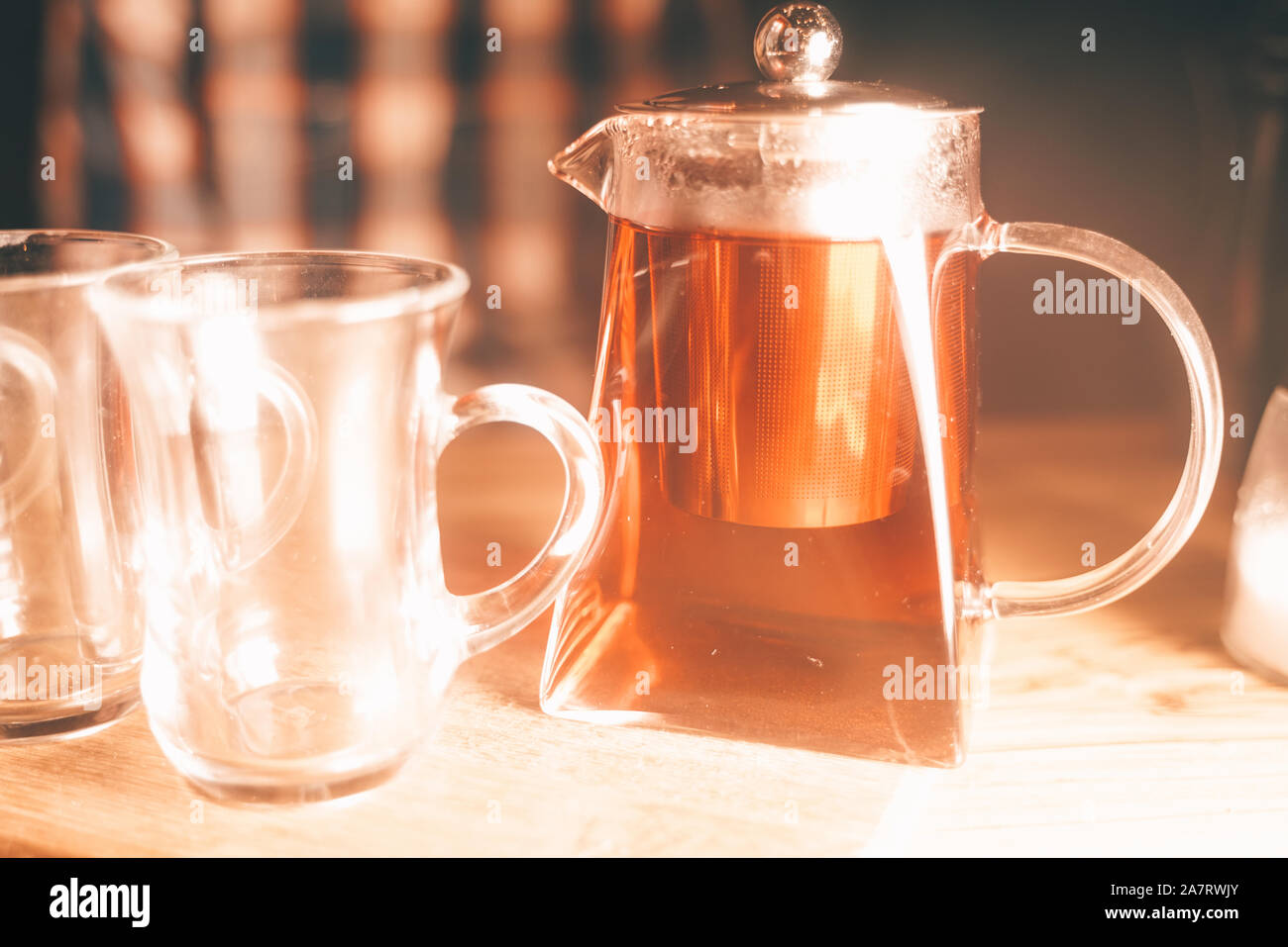 teen boy pours hot tea in transparent teapot into cups on table on dark ...