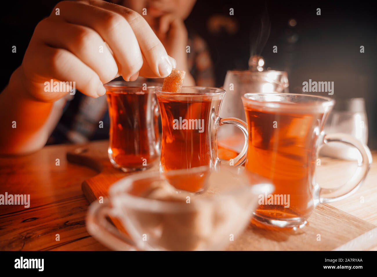 teen boy pours hot tea in transparent teapot into cups on table on dark ...