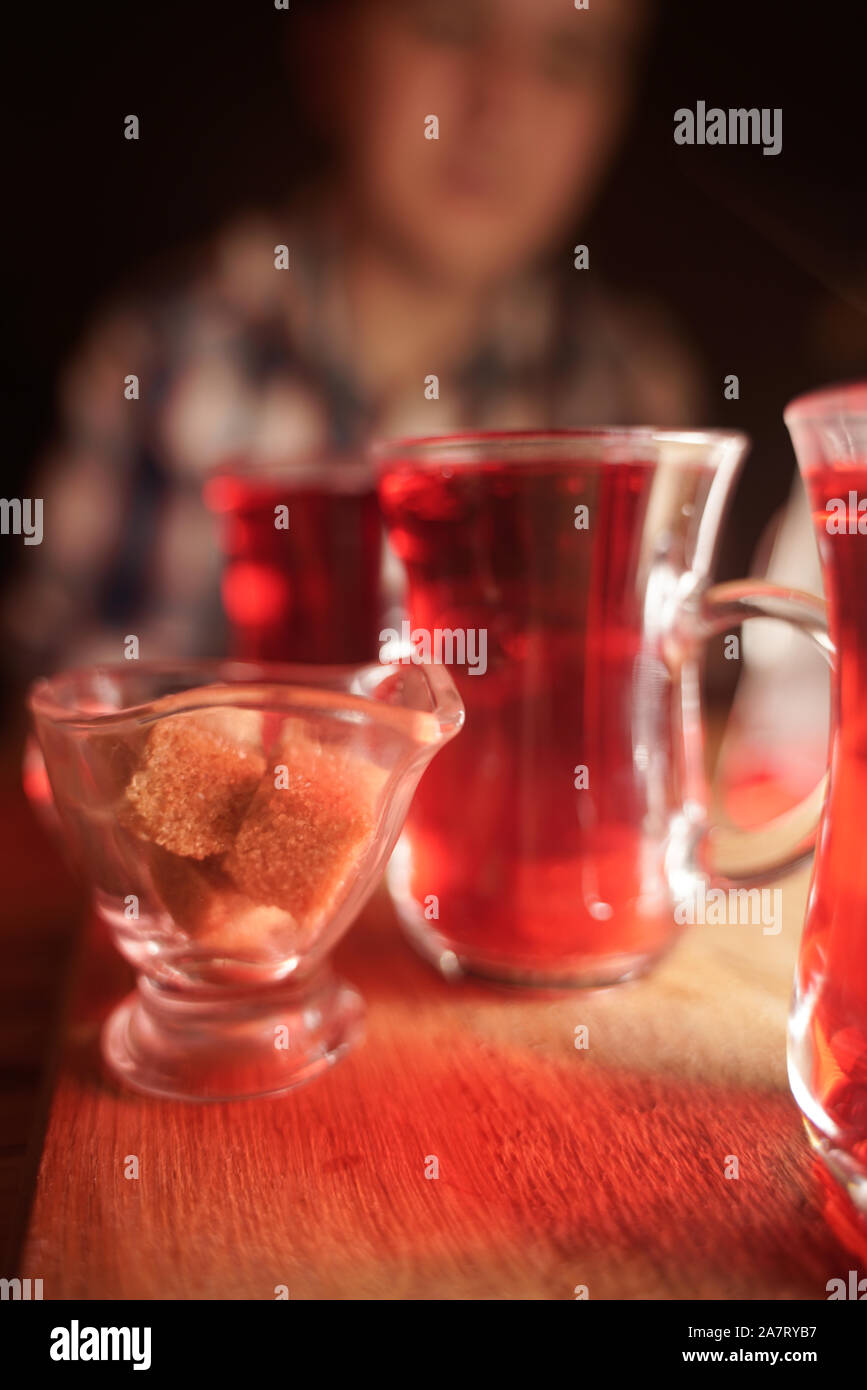 teen boy pours hot tea in transparent teapot into cups on table on dark ...