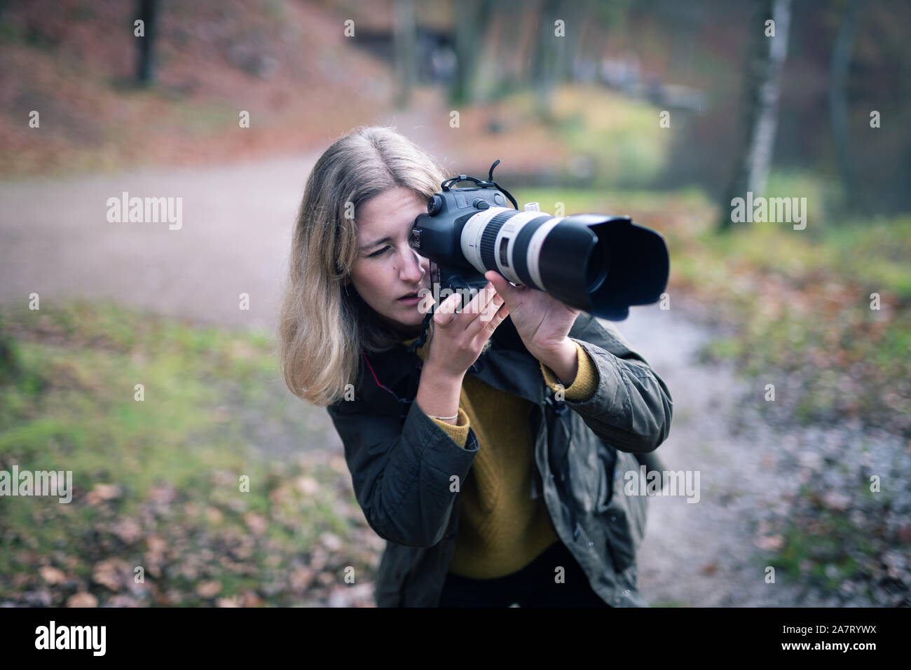 Blonde photographer squatting and using camera with large telephoto ...