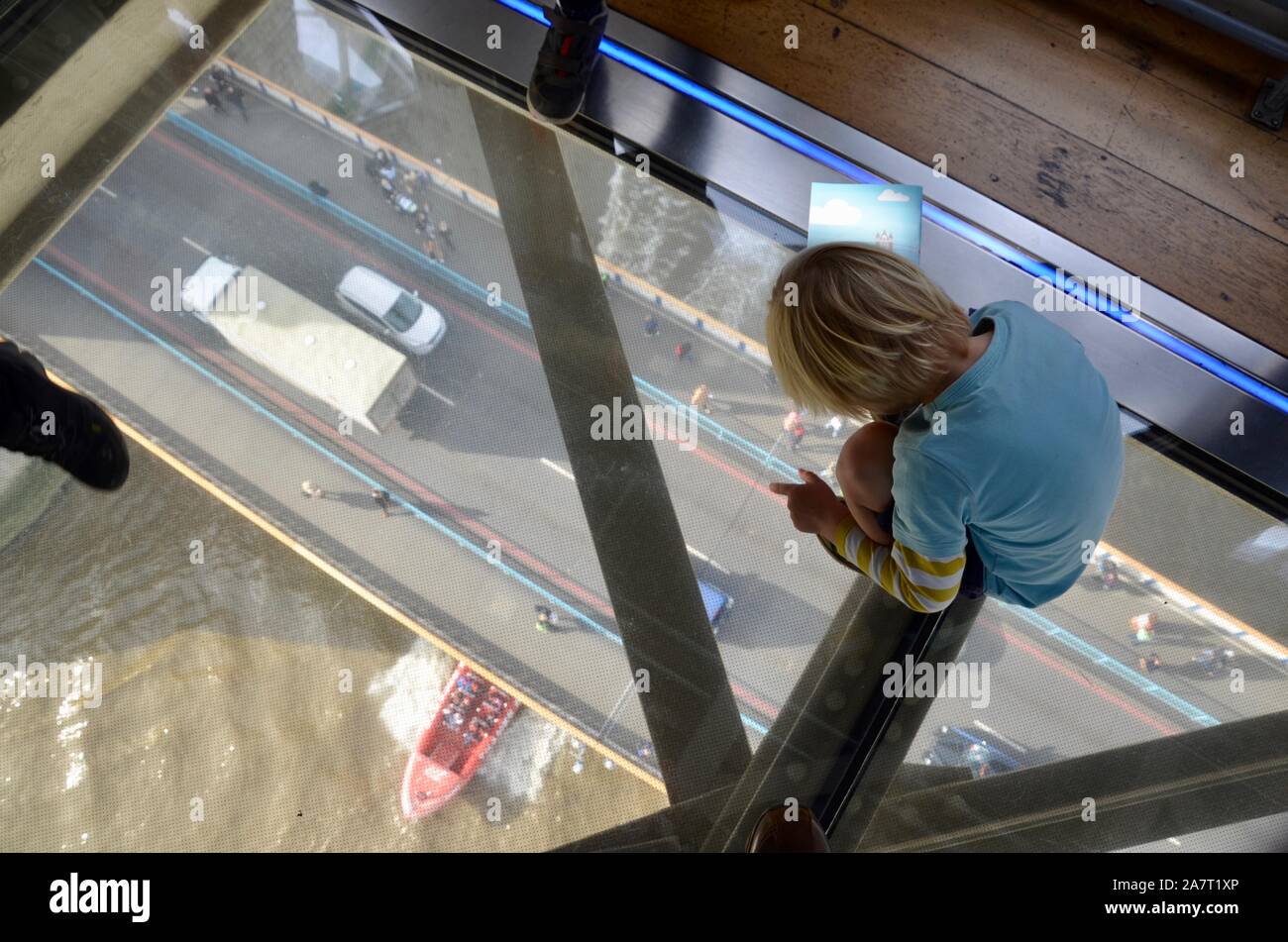 Young boy looking down through glass walkway of Tower Bridge at busy ...