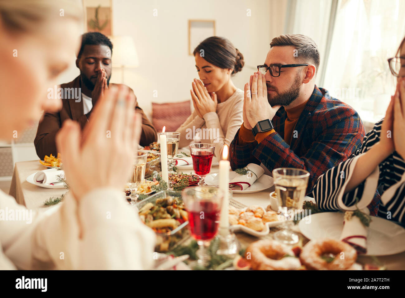 Multi-ethnic group of elegant adult people praying sitting at dinner ...