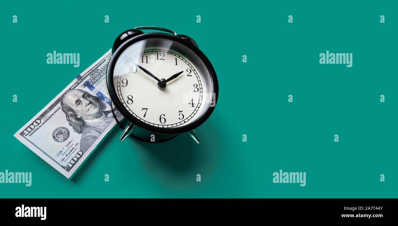 Alarm clock lying on a stack money on green background with copyspace ...