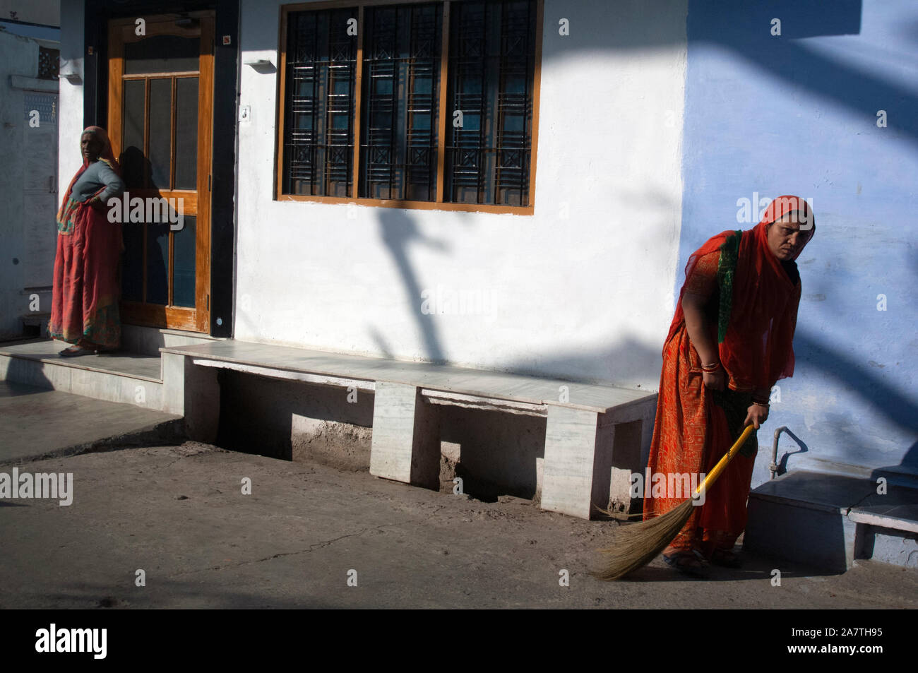 Two Indian women are sweeping the floor outside their house in Udaipur ...