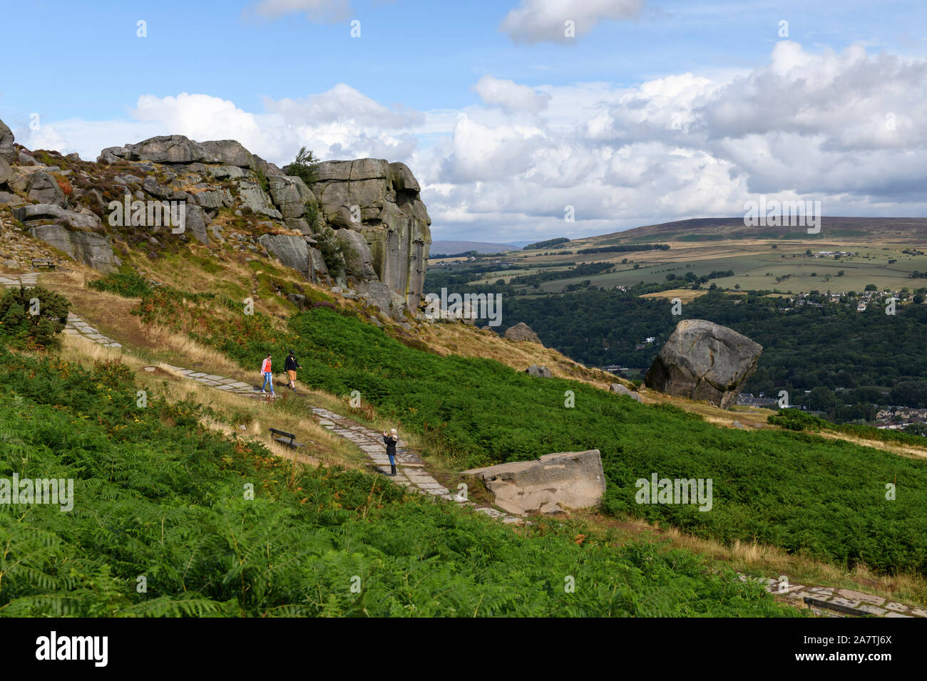 People walking on path by high sunlit rocky outcrop (valley below ...