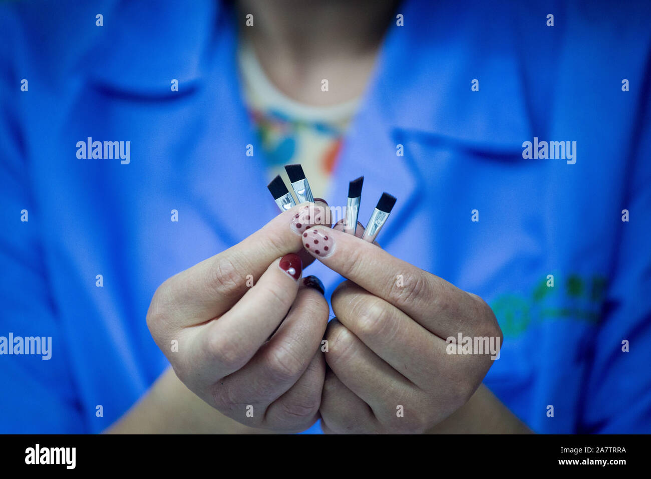 A Chinese female worker shows makeup brushes on an assembly line at a ...