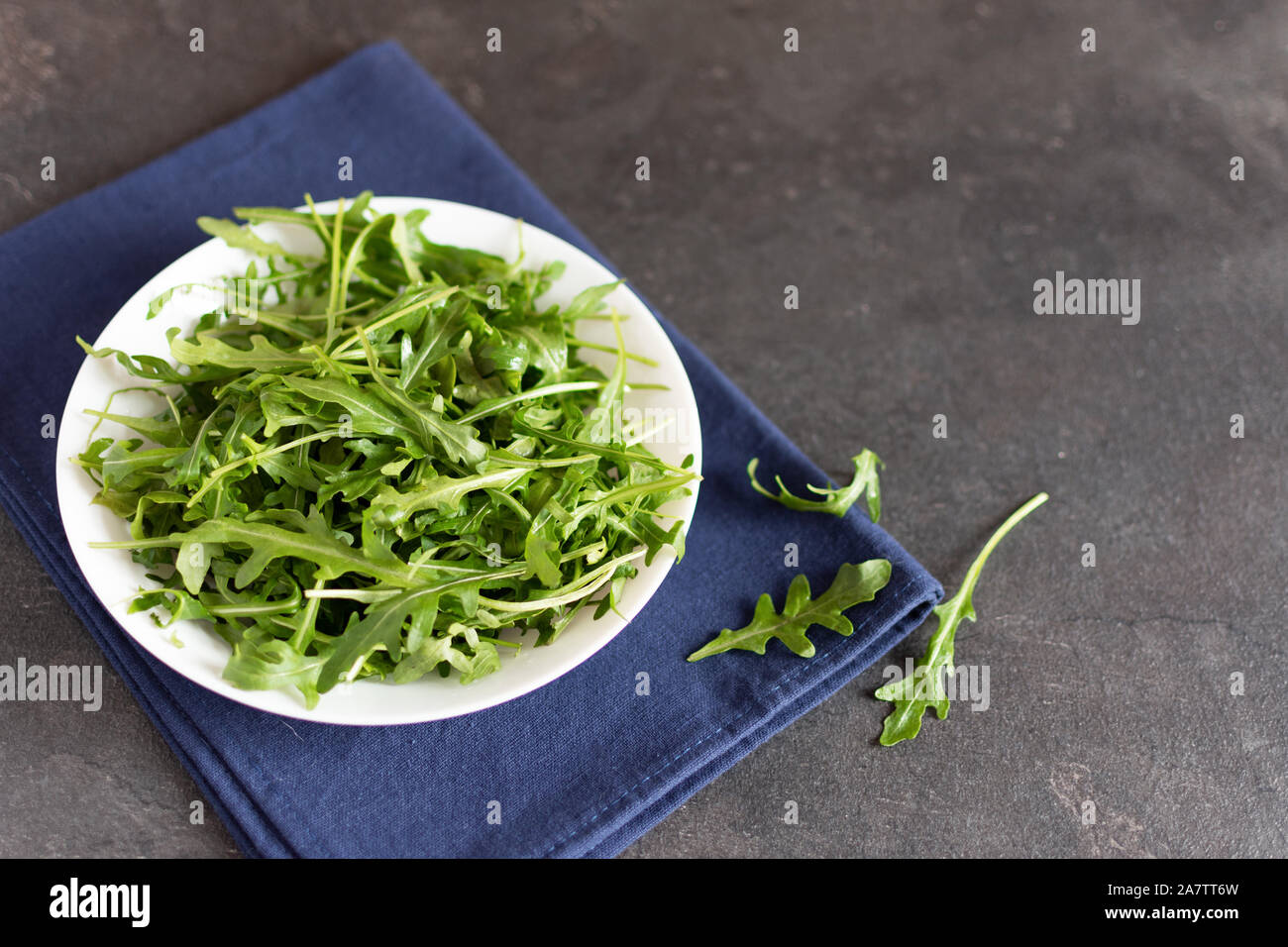 Fresh green arugula in a white ceramic bowl on black table. Arugula is ...