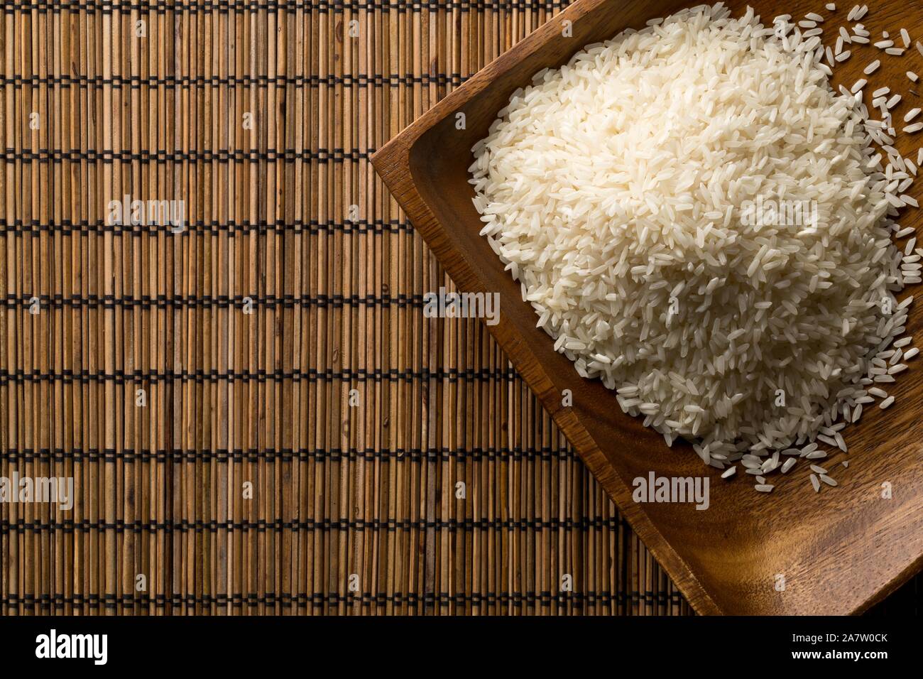 White uncooked, raw long grain rice in wooden bowl on bamboo mat with ...