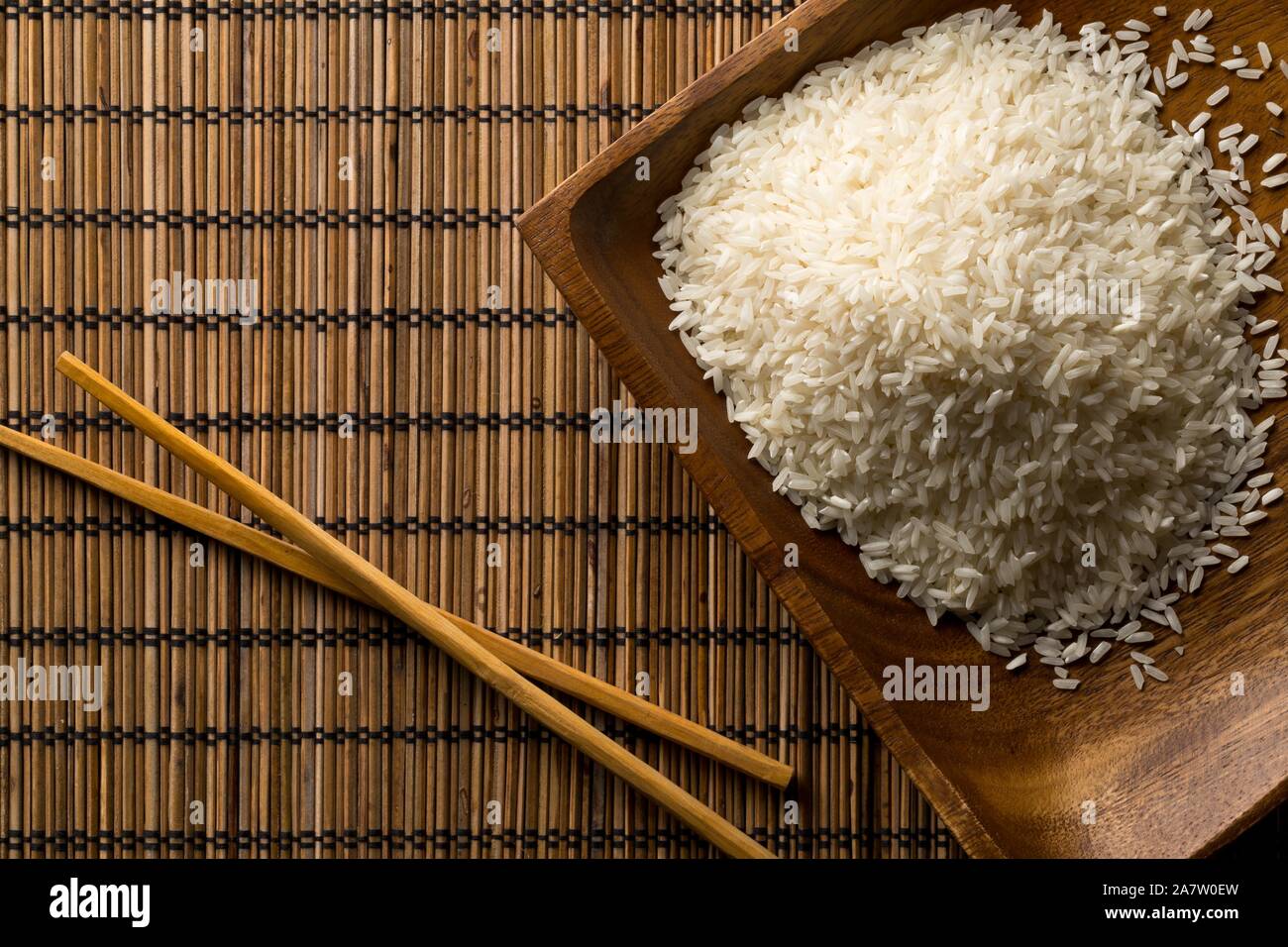 White uncooked, raw long grain rice in wooden bowl with chopsticks on ...