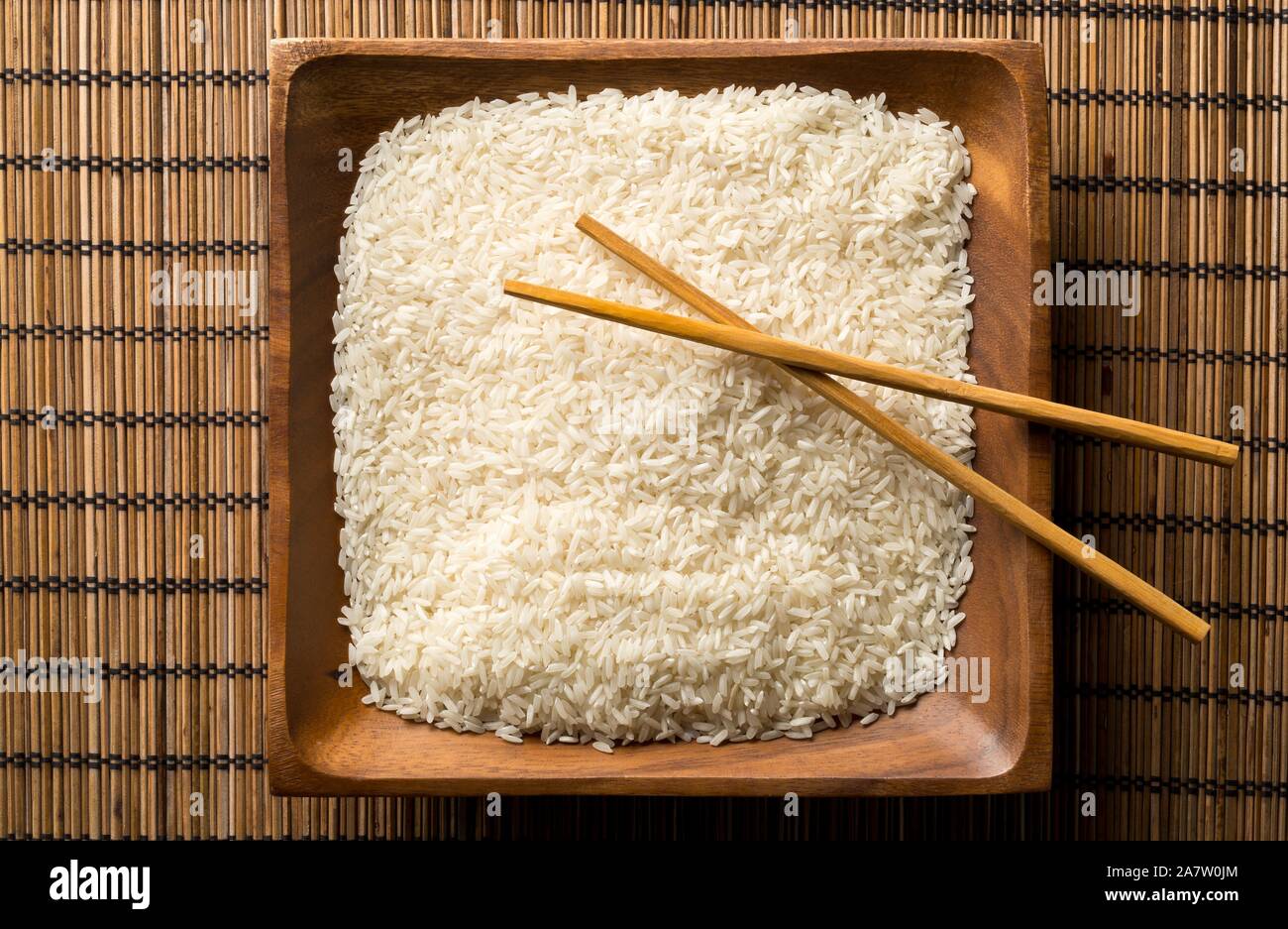 White uncooked, raw long grain rice on wooden plate with chopsticks on ...