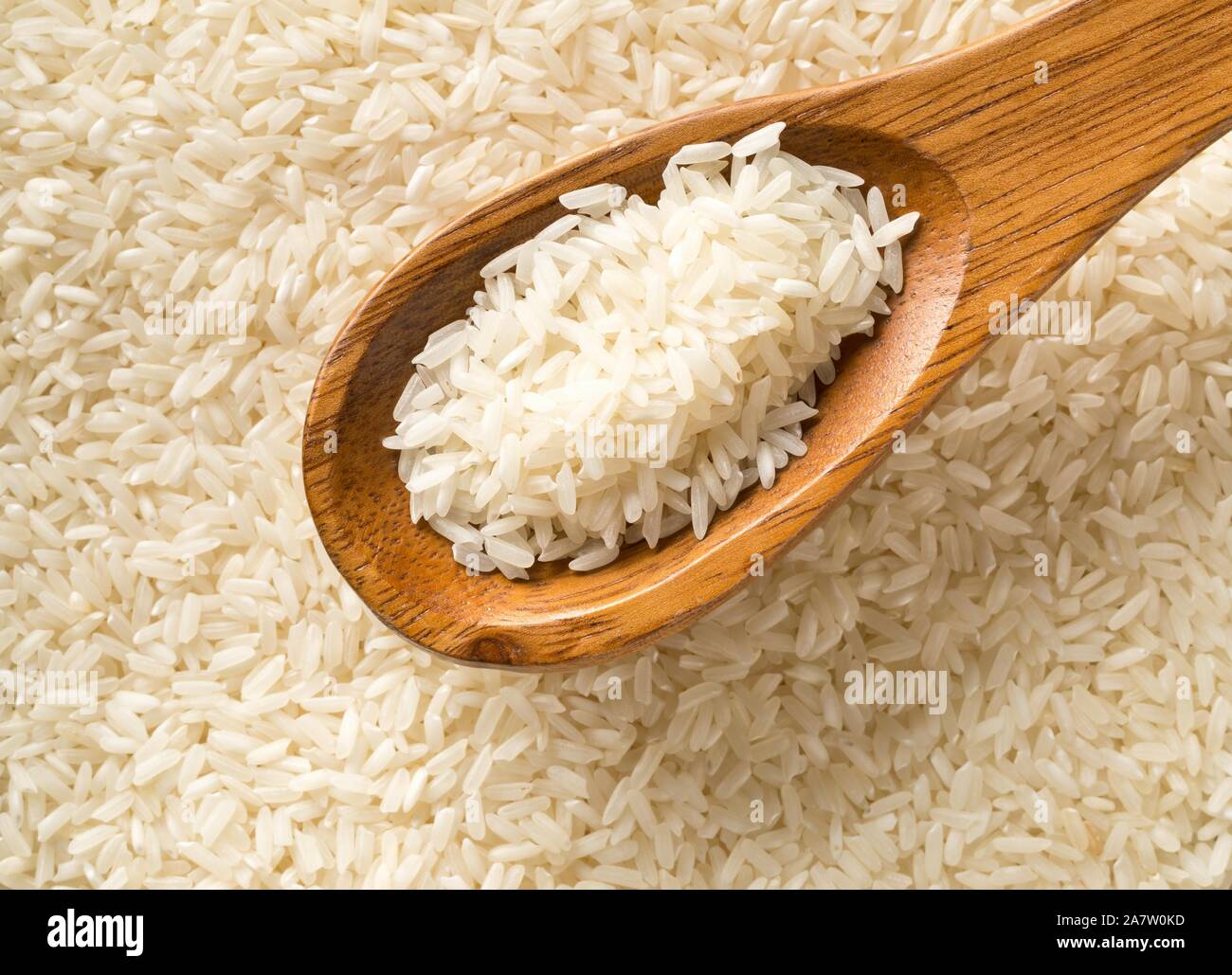 White uncooked, raw long grain rice full frame with wooden spoon top ...