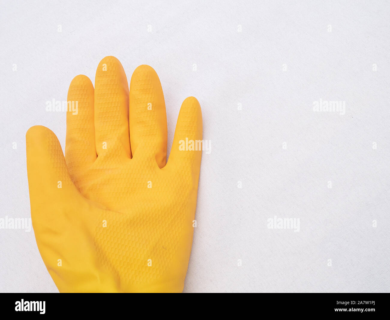 Hands wearing bright yellow rubber gloves on a white cloth background ...