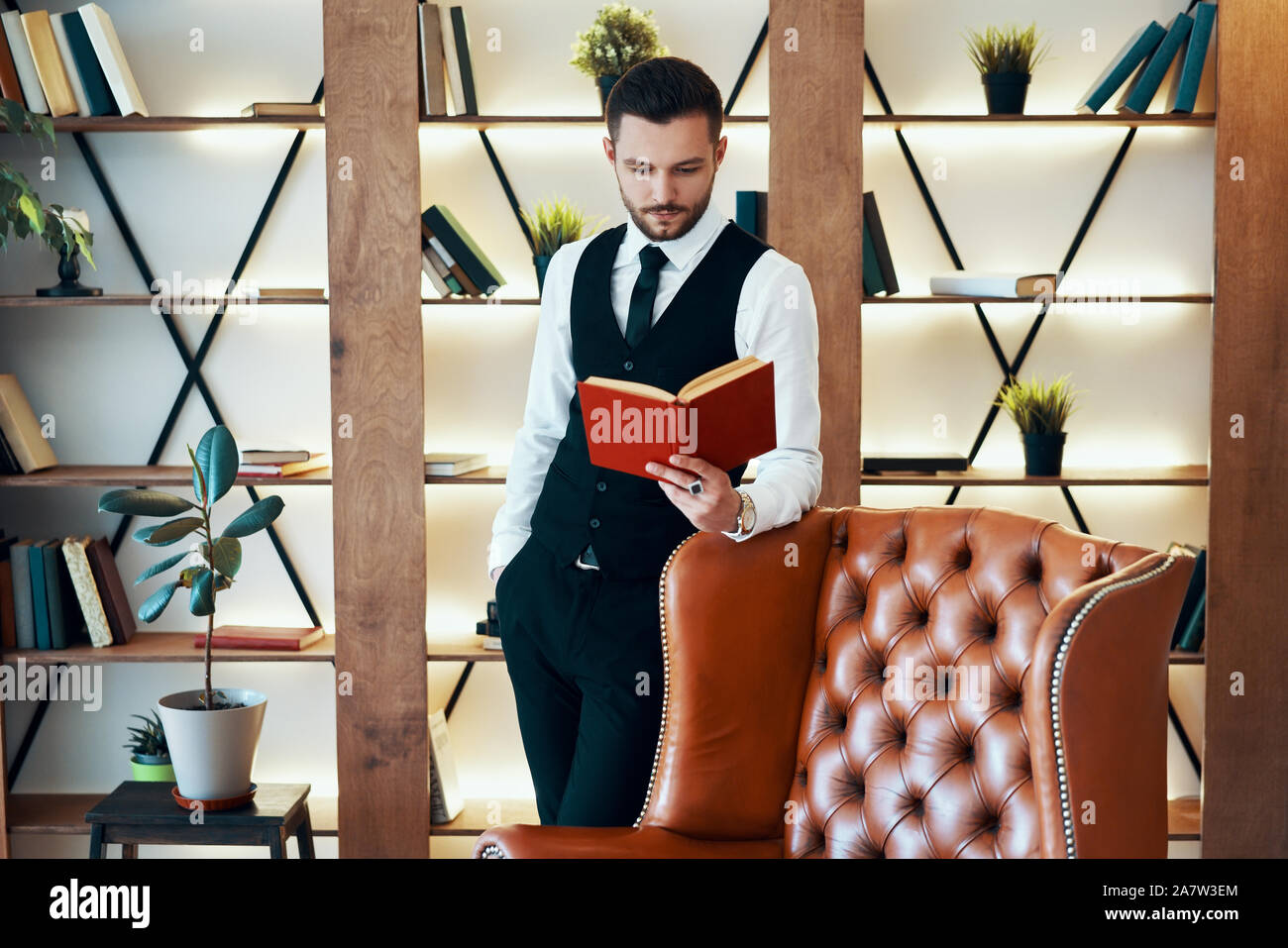 Handsome young man in elegant suit reading a book in modern luxury ...