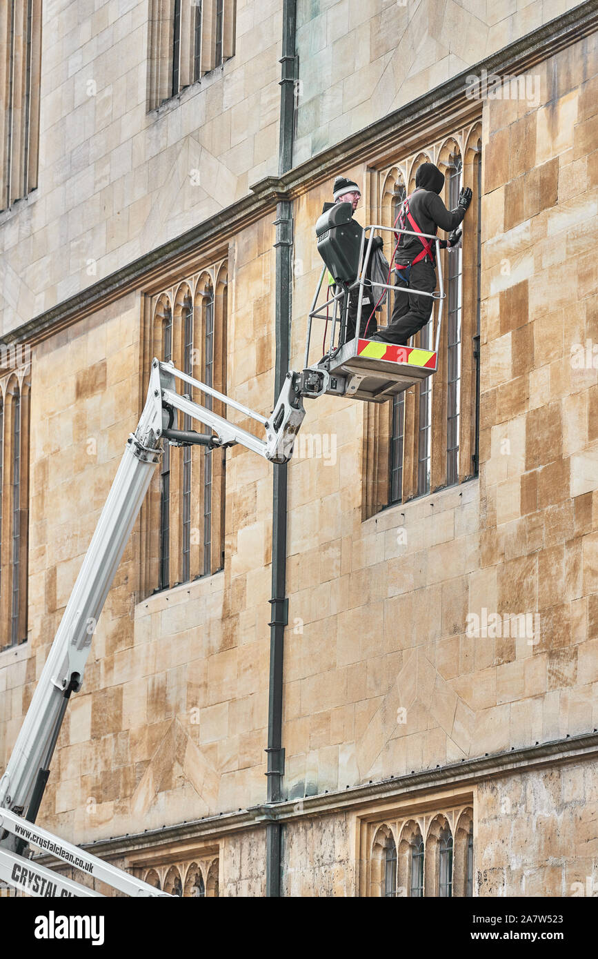 Two male window cleaners use a derrick to clean the outside windows of ...