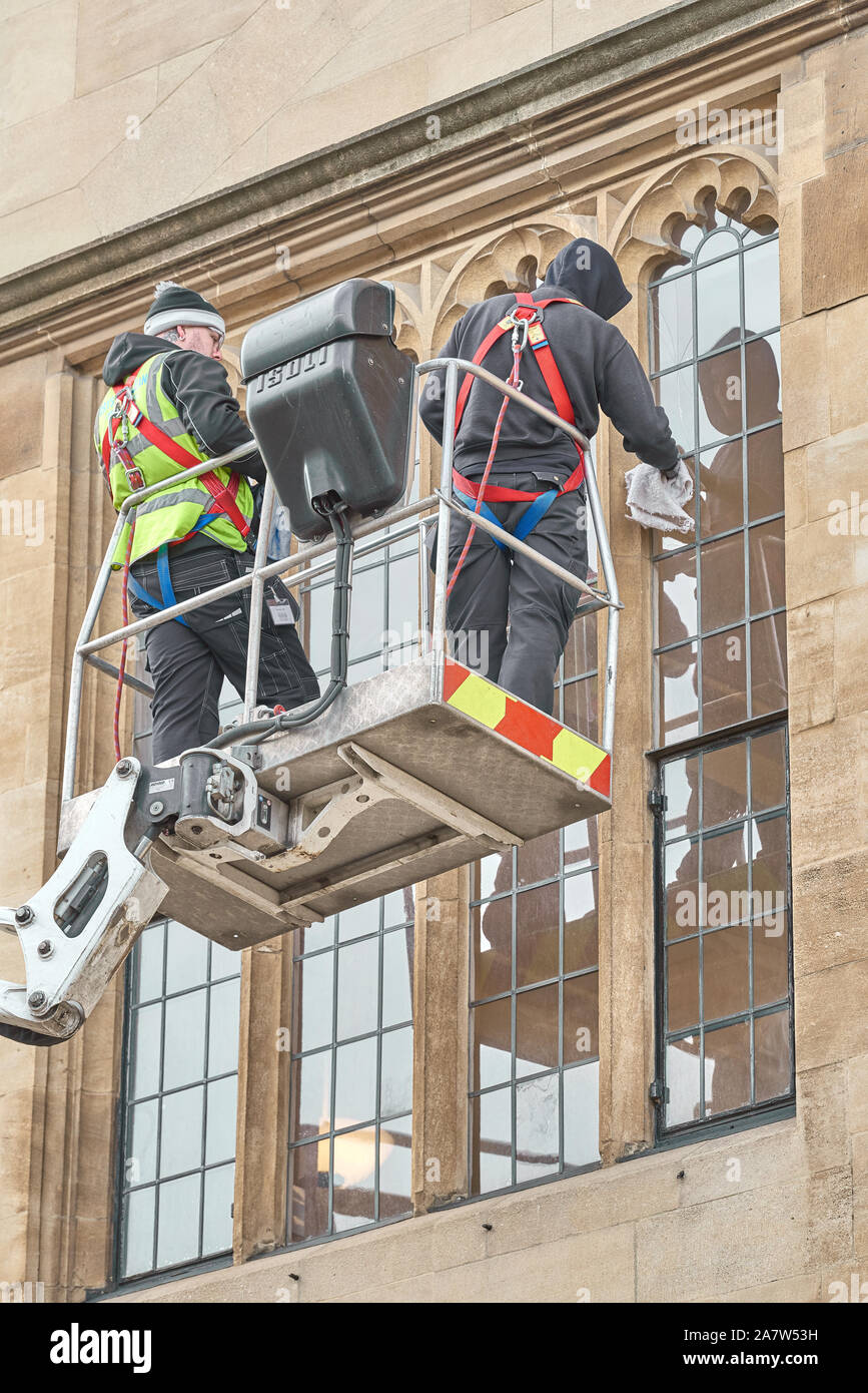 Two male window cleaners use a derrick to clean the outside windows of ...