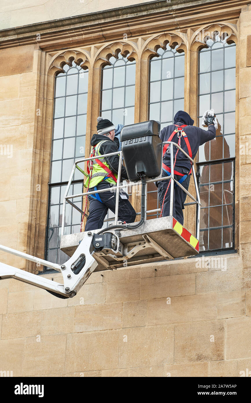 Two male window cleaners use a derrick to clean the outside windows of ...