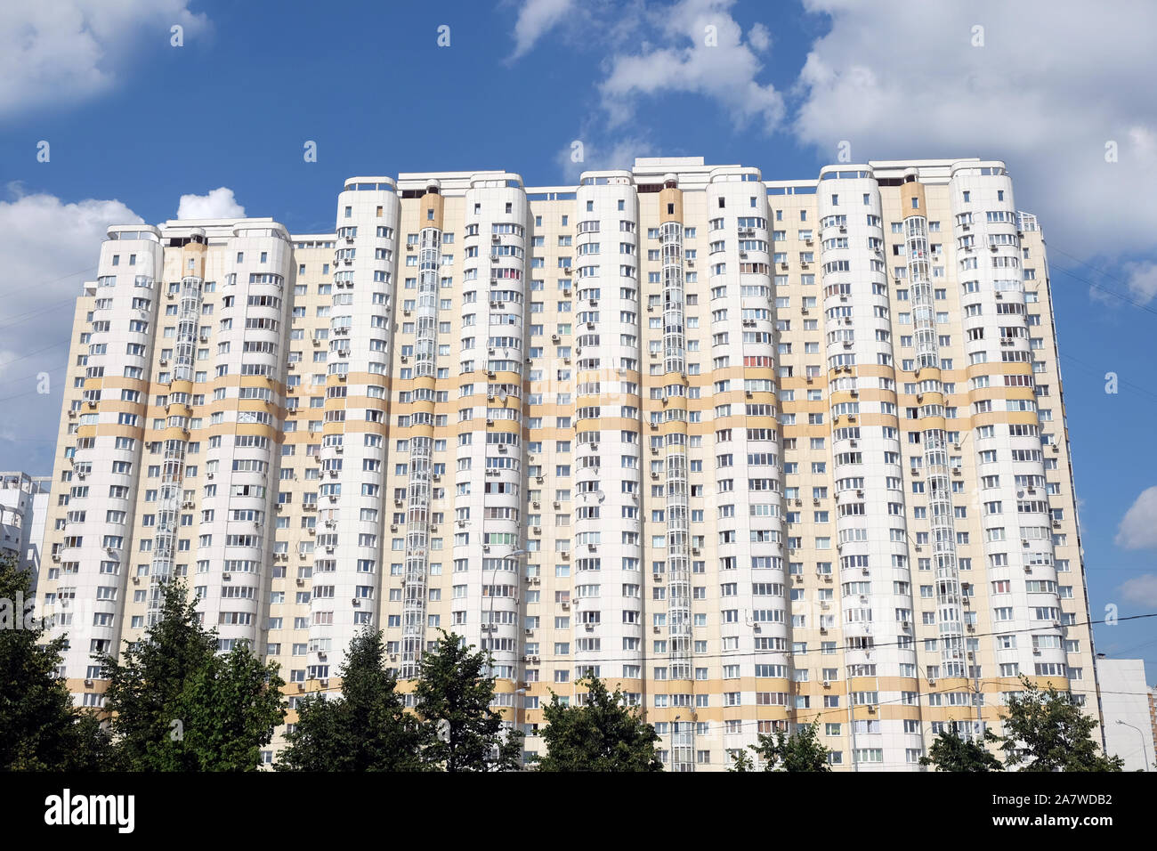 Facade of high modern beige residential building on blue sky with white ...