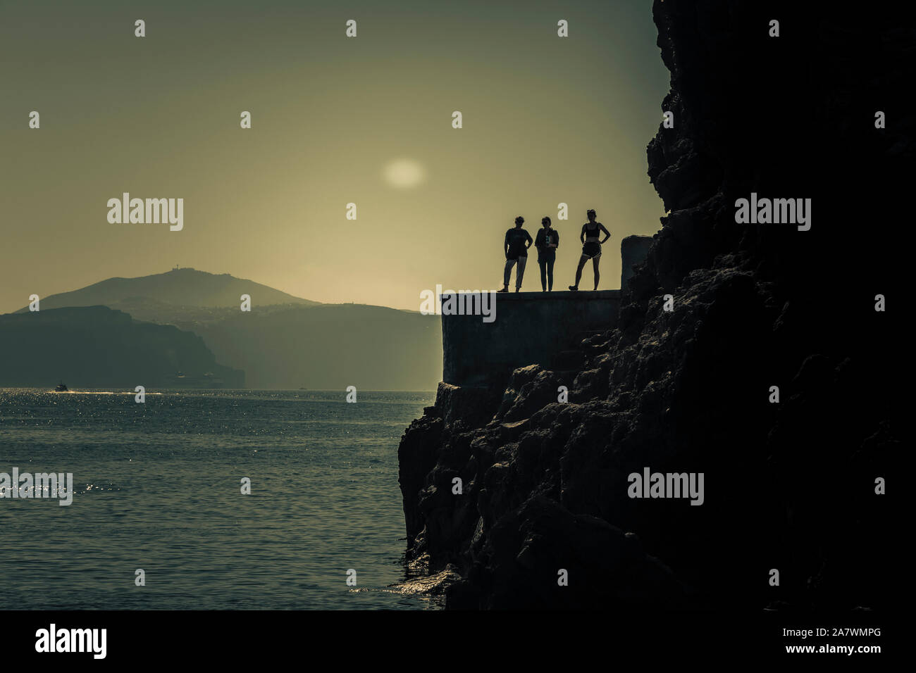 Tourists jumping off a large rock ledge in Amoudi Bay on Santorini ...
