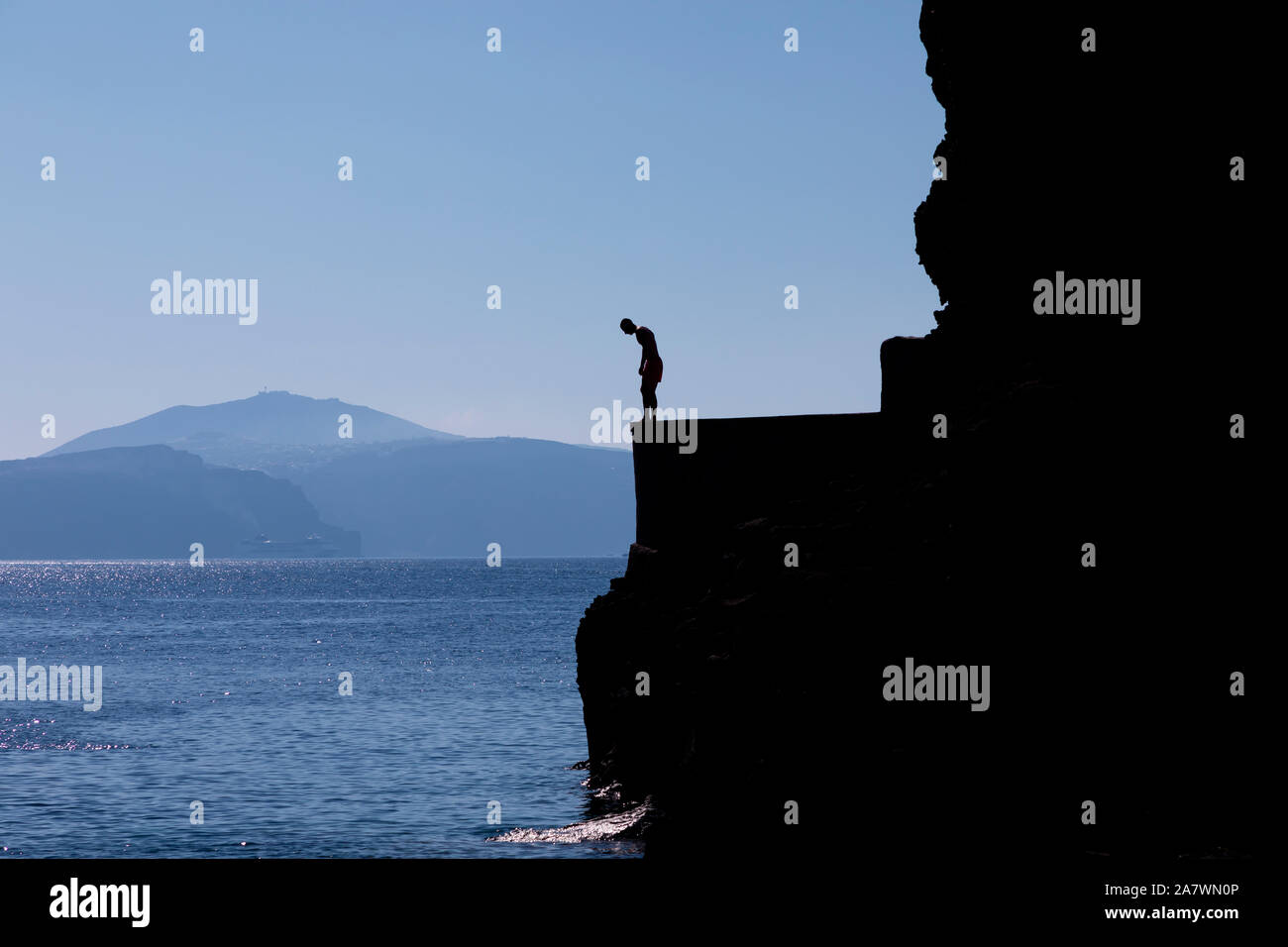 Tourists jumping off a large rock ledge in Amoudi Bay on Santorini ...