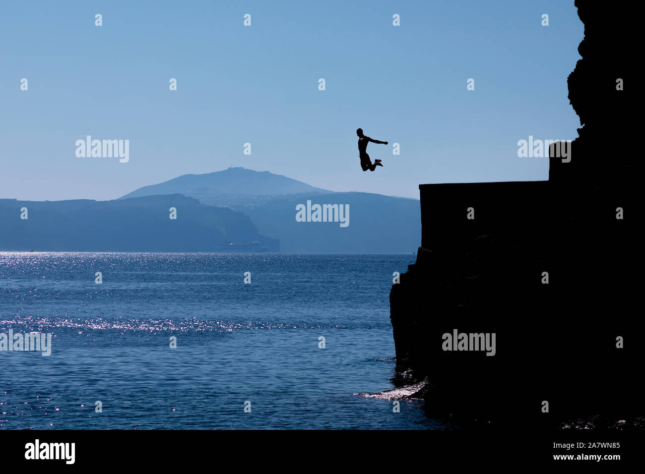 Tourists jumping off a large rock ledge in Amoudi Bay on Santorini ...