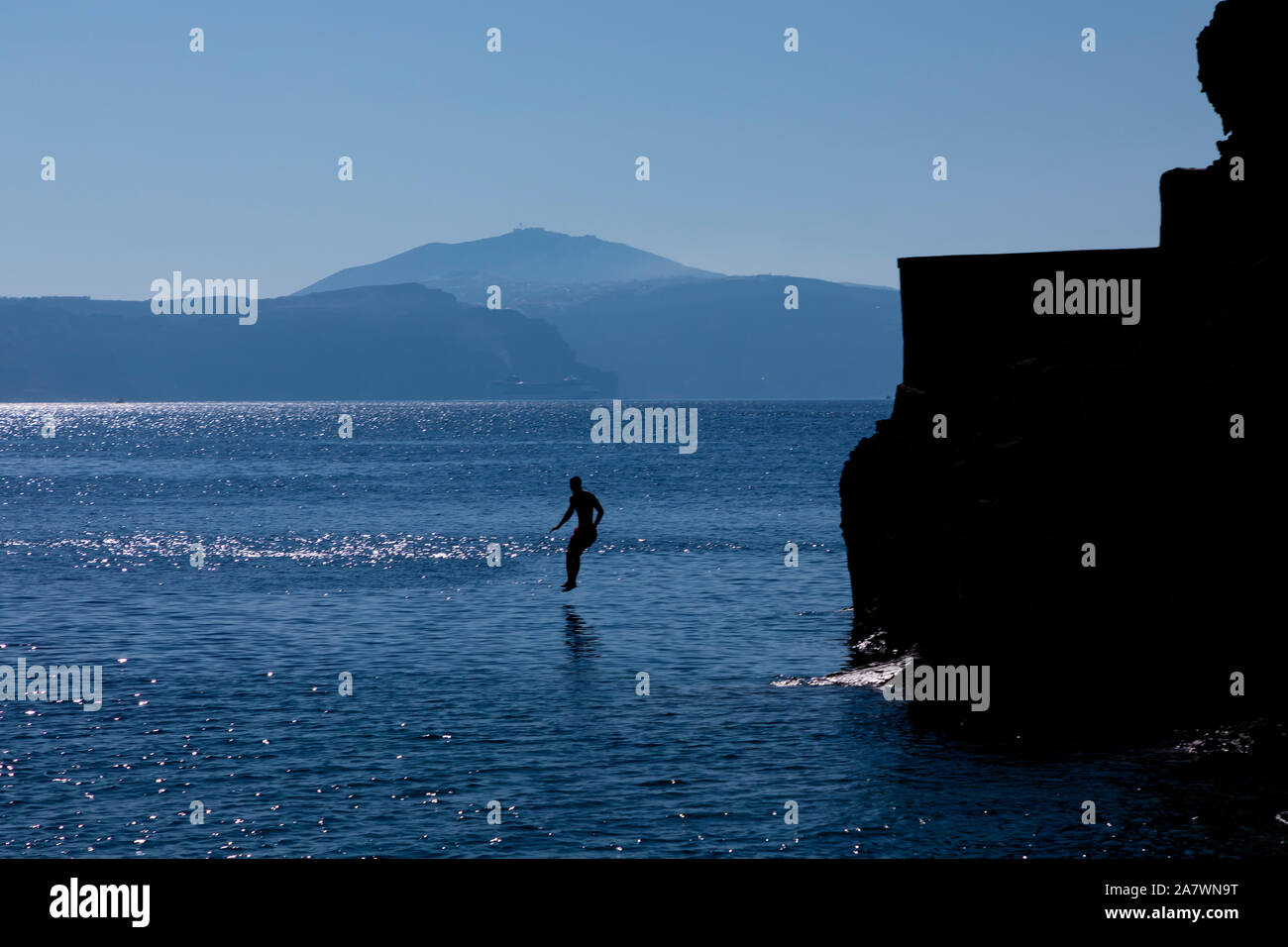 Tourists jumping off a large rock ledge in Amoudi Bay on Santorini ...