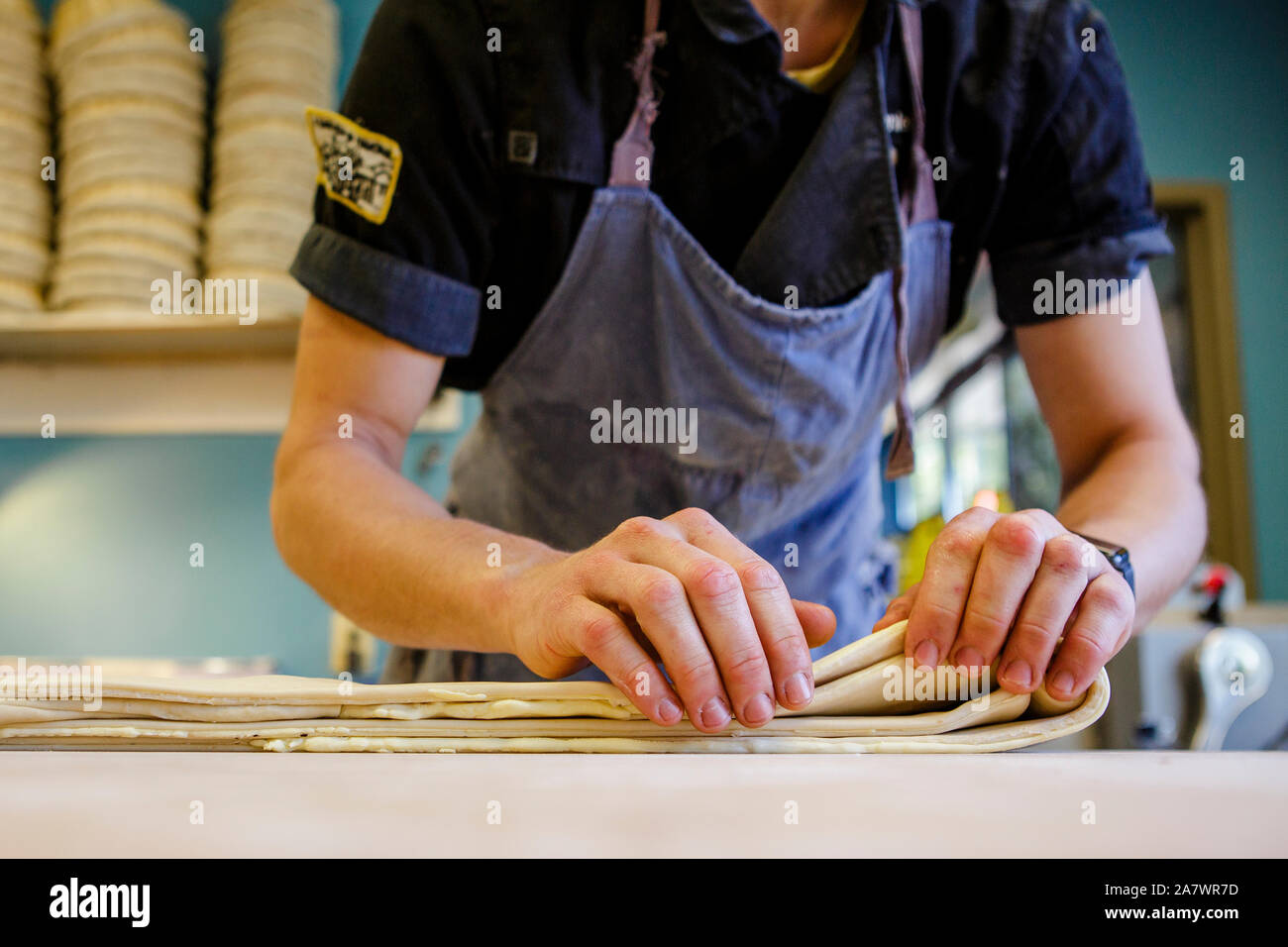 Close-up view of a baker folding buttered pastry dough on a countertop ...