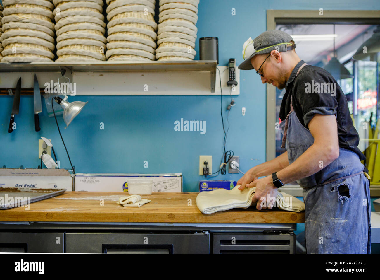 A smiling professional baker folds pastry dough on a floured counter ...