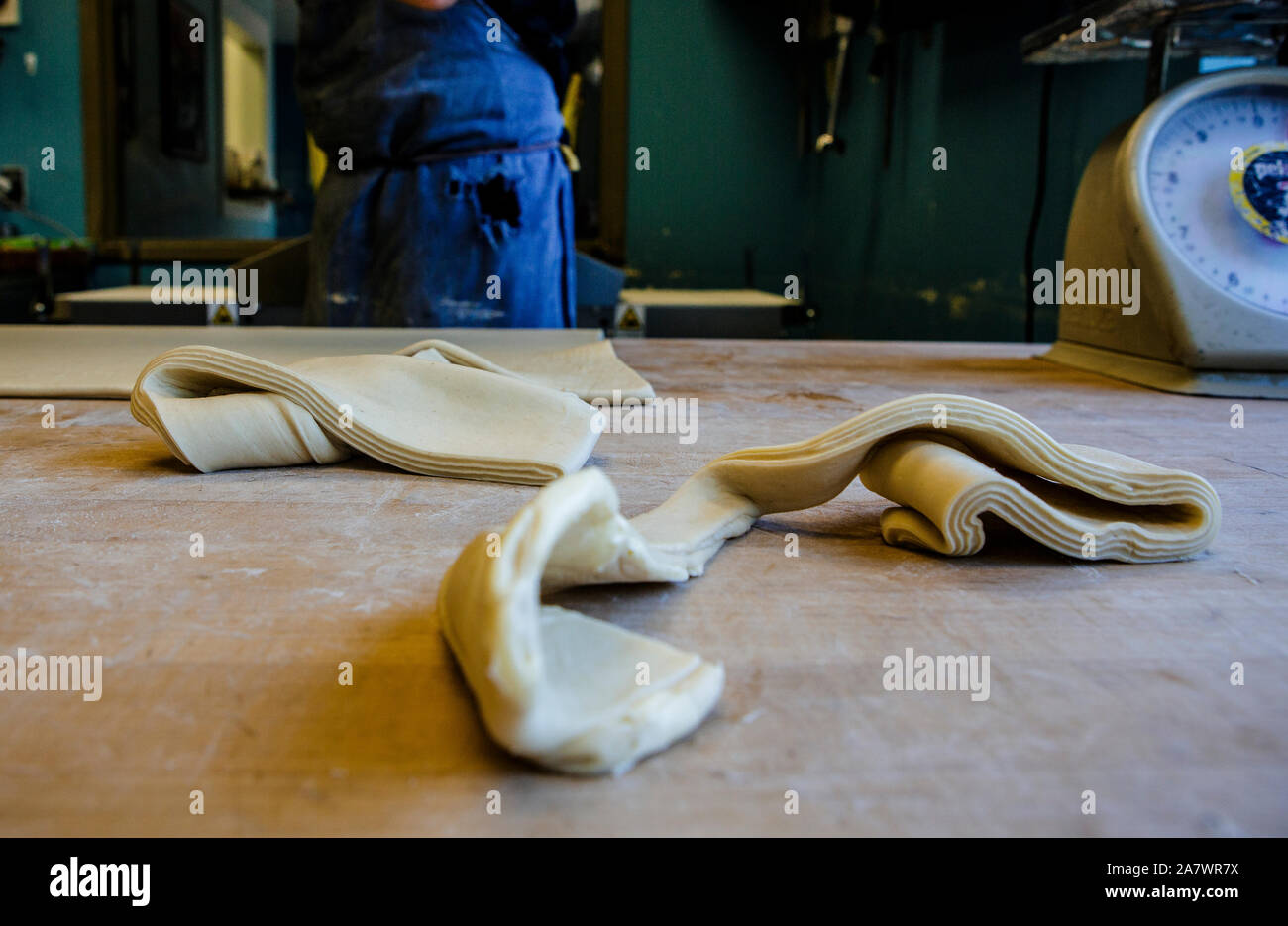 strips of pastry dough lay on floured wooden counter in bakery kitchen ...