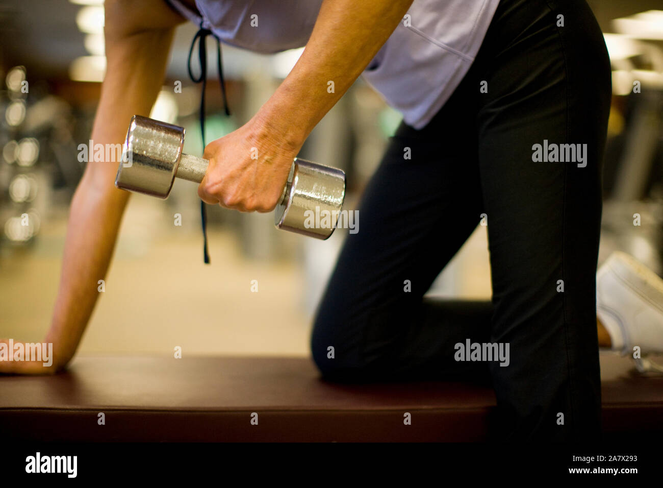 Woman's arm lifting a hand weight while kneeling on a bench inside a ...